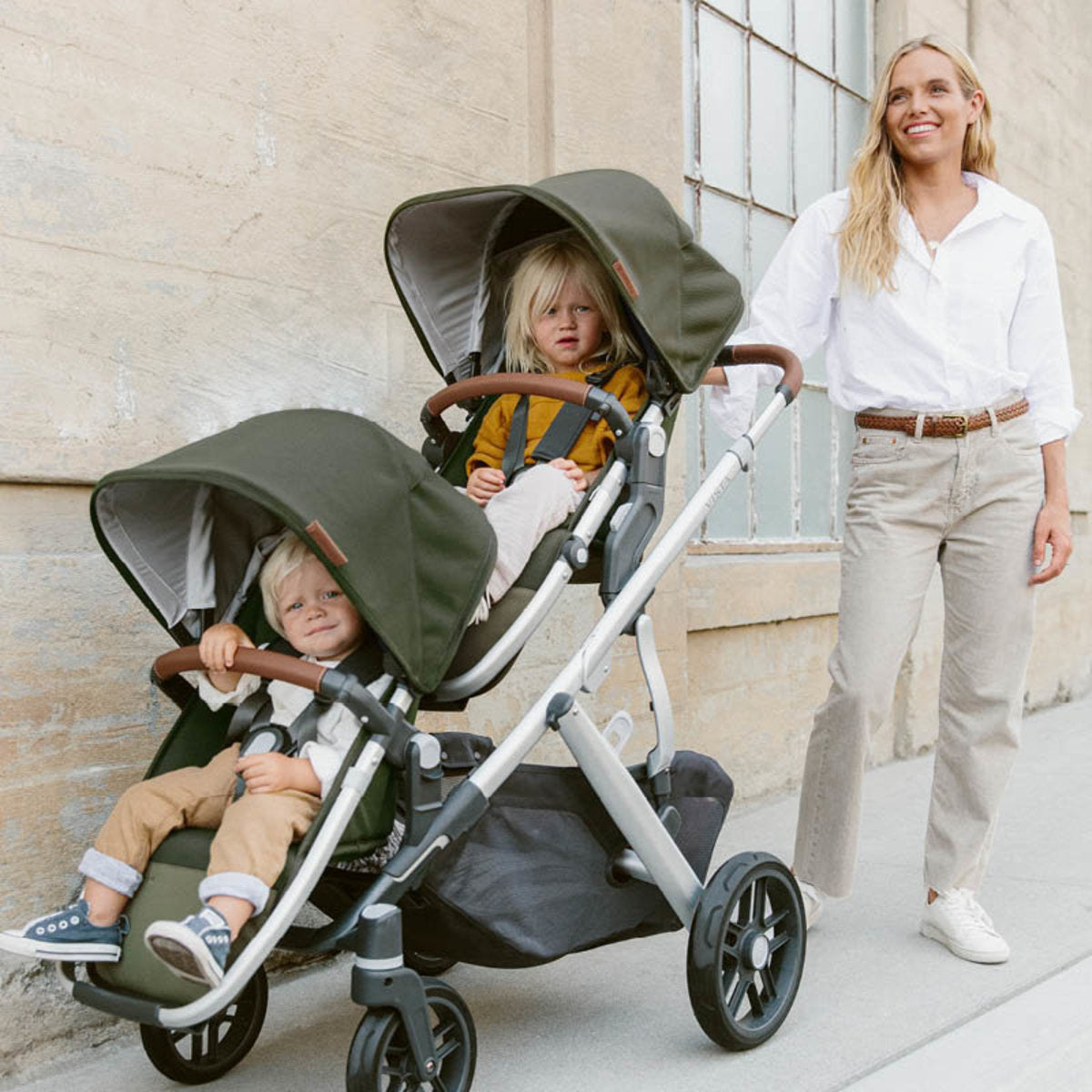 Mother pushing a double stroller with two toddlers on a city sidewalk ...